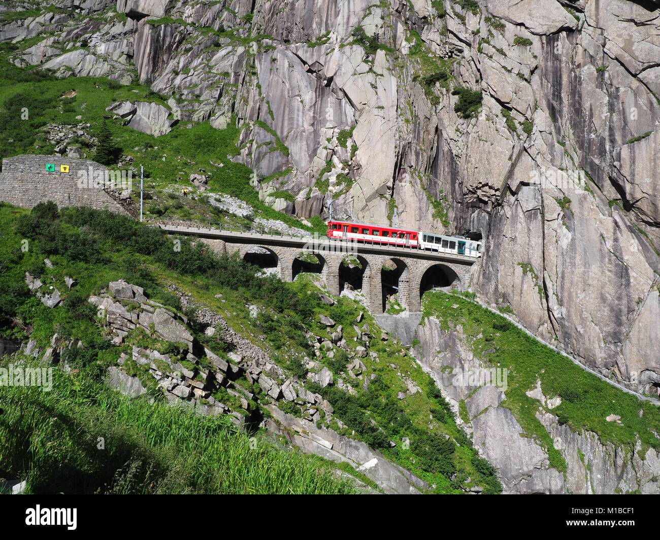 Red express train on scenic stony St. Gotthard railway bridge and ...