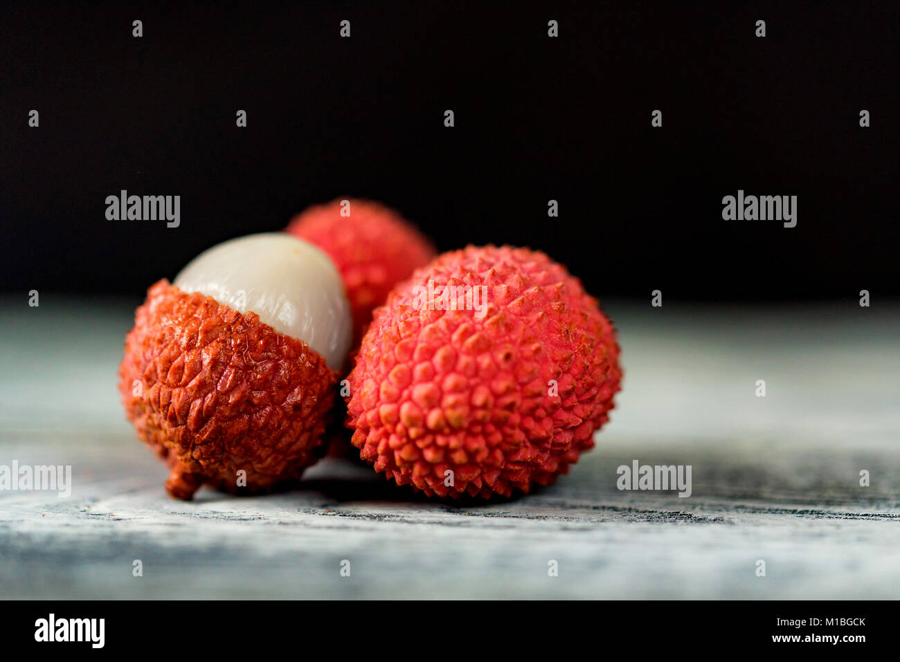 Three lychee fruits on dark background close Stock Photo - Alamy