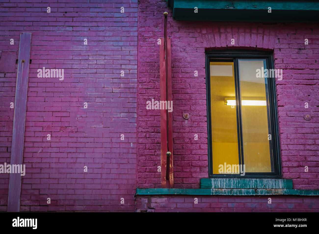 A dim light window in a purple brick wall building on a street of old ...