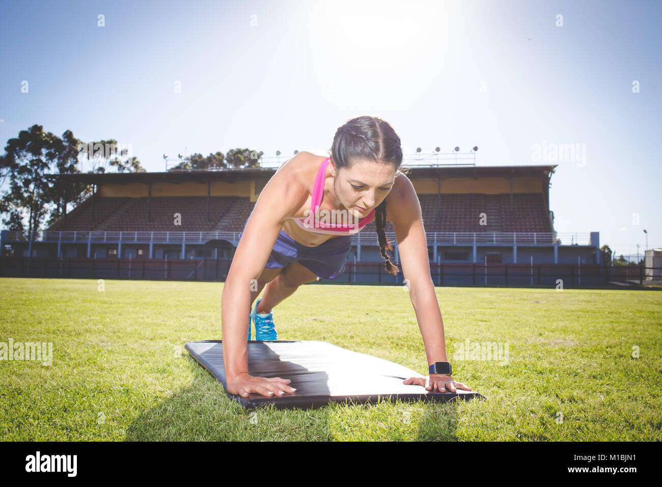 Female fitness model doing exercises outside at a sport stadium on a ...