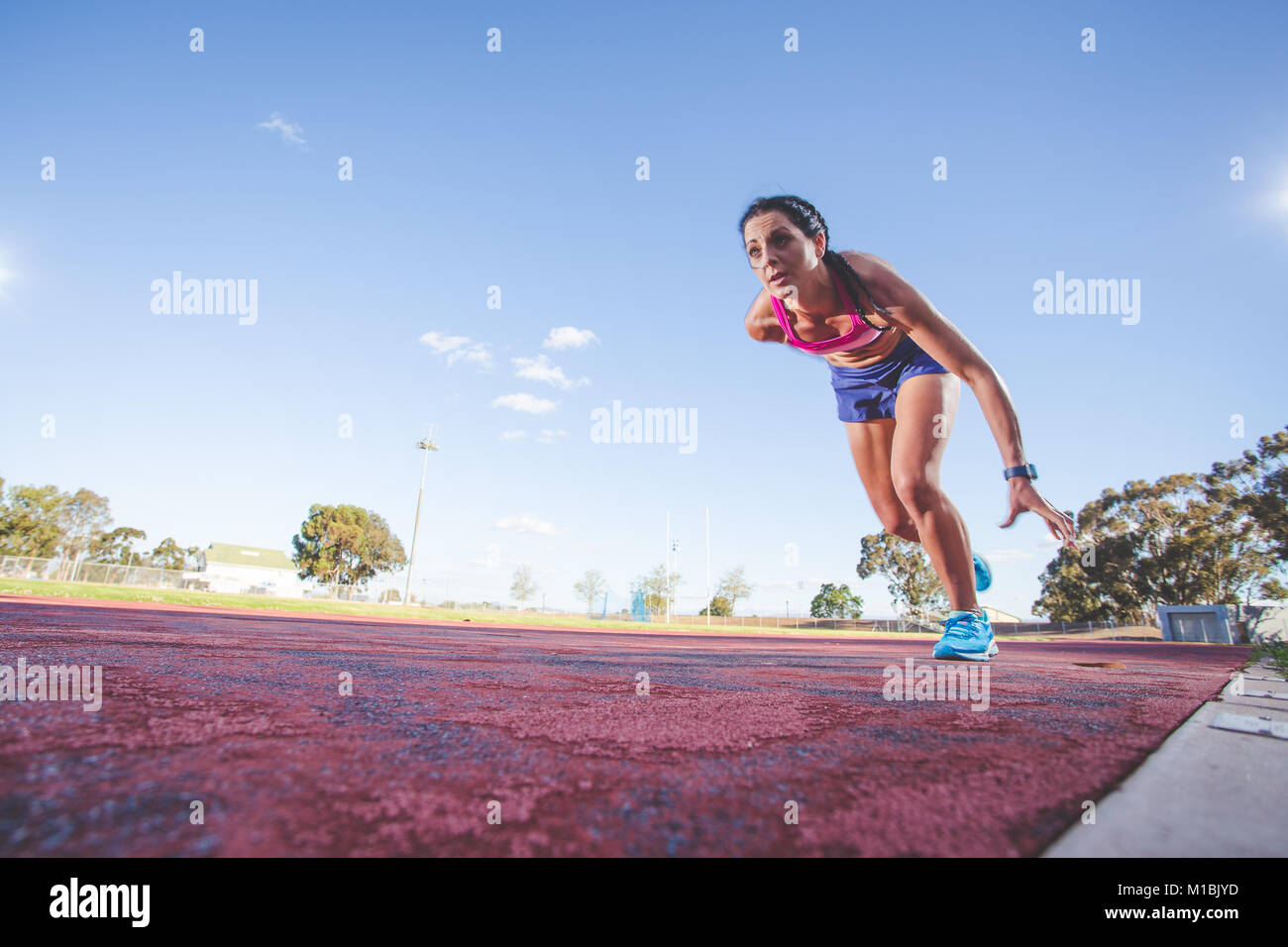 Female fitness model and track athlete sprinting on an athletics track ...