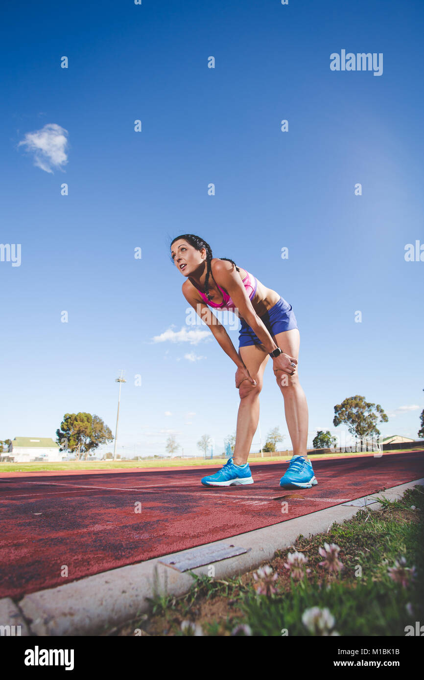Female fitness model and track athlete sprinting on an athletics track ...