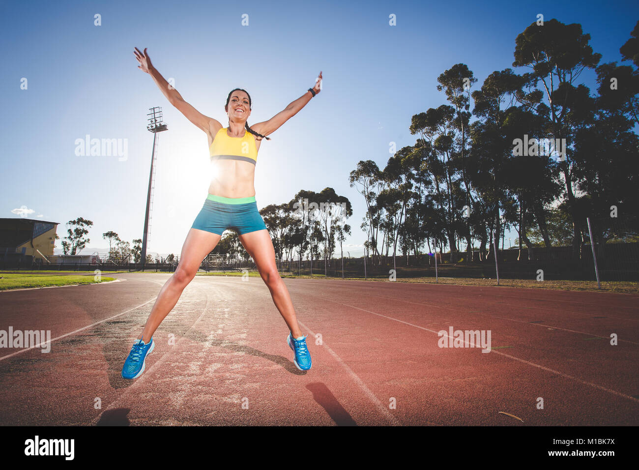 Female fitness model and track athlete sprinting on an athletics track ...