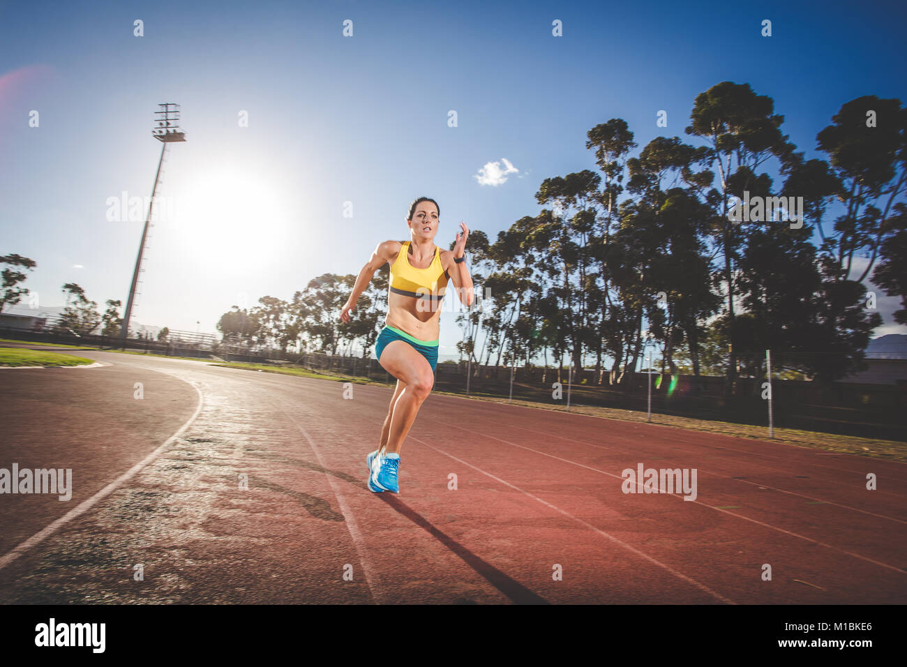 Female fitness model and track athlete sprinting on an athletics track ...