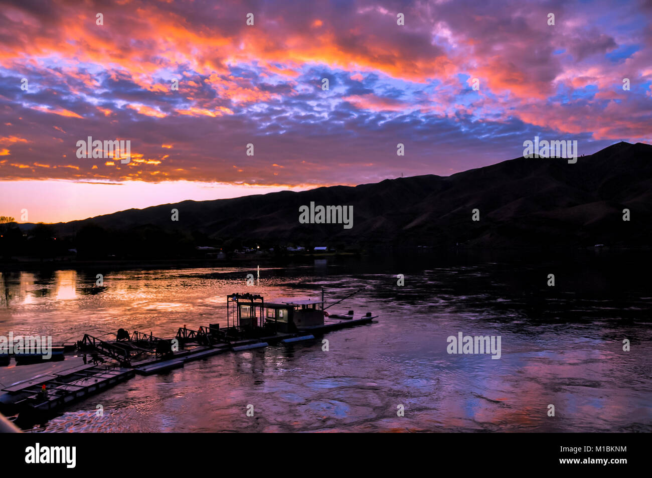Dramatic sunset landscape with lake, sky reflection, boat and foothills ...