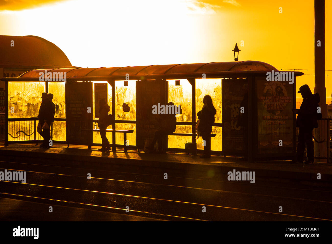 Silhouetted figures in a bus stop during a sunset on Blackpool seafront ...