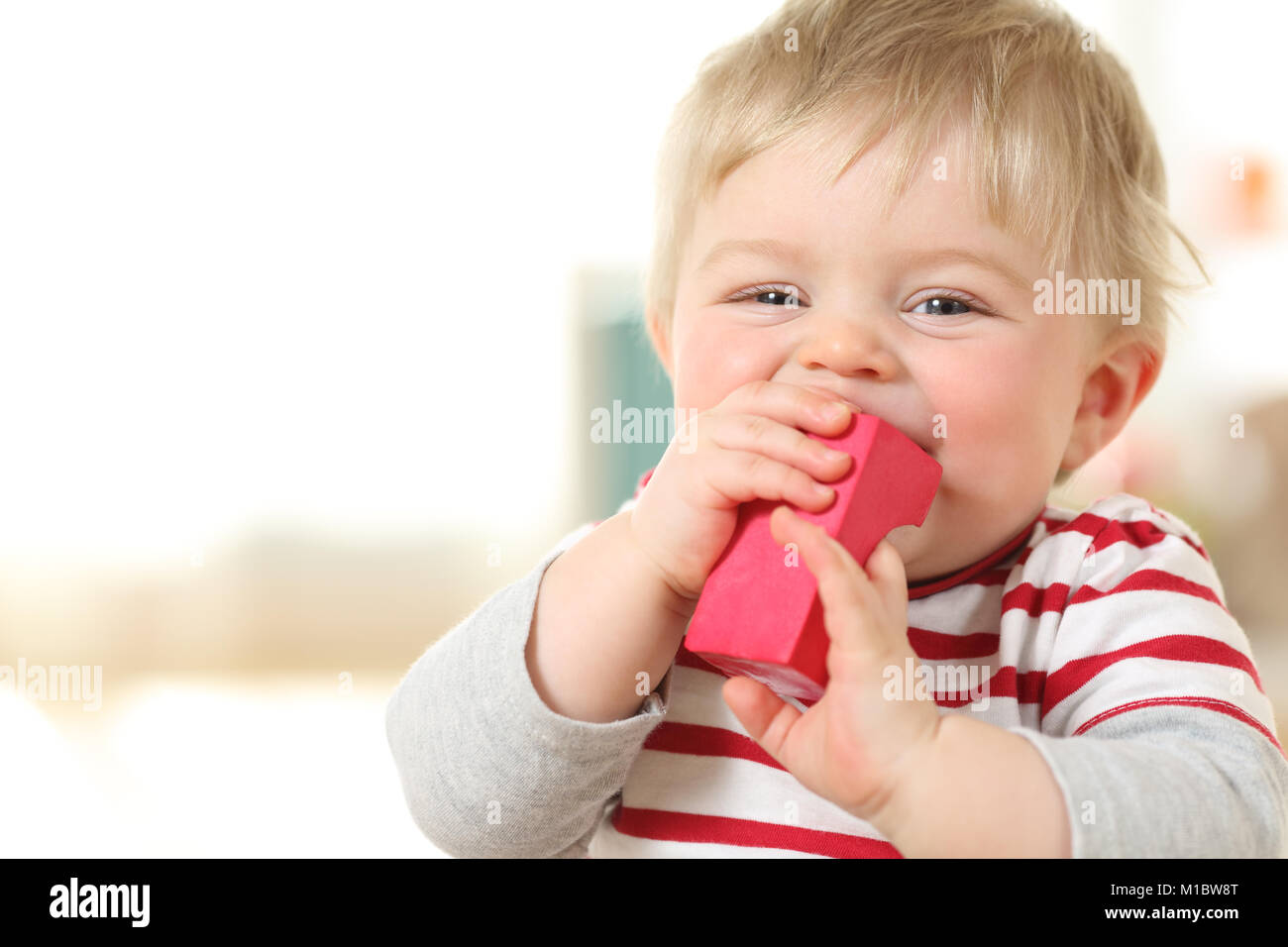 Cheerful baby biting a toy an looking you at home Stock Photo - Alamy
