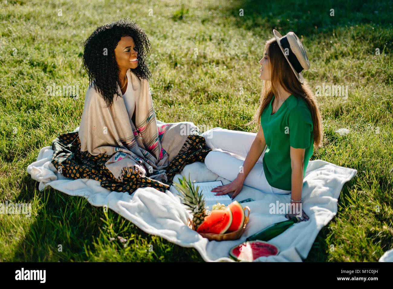 Beautiful two multi-race female friends are happily talking on a picnic ...