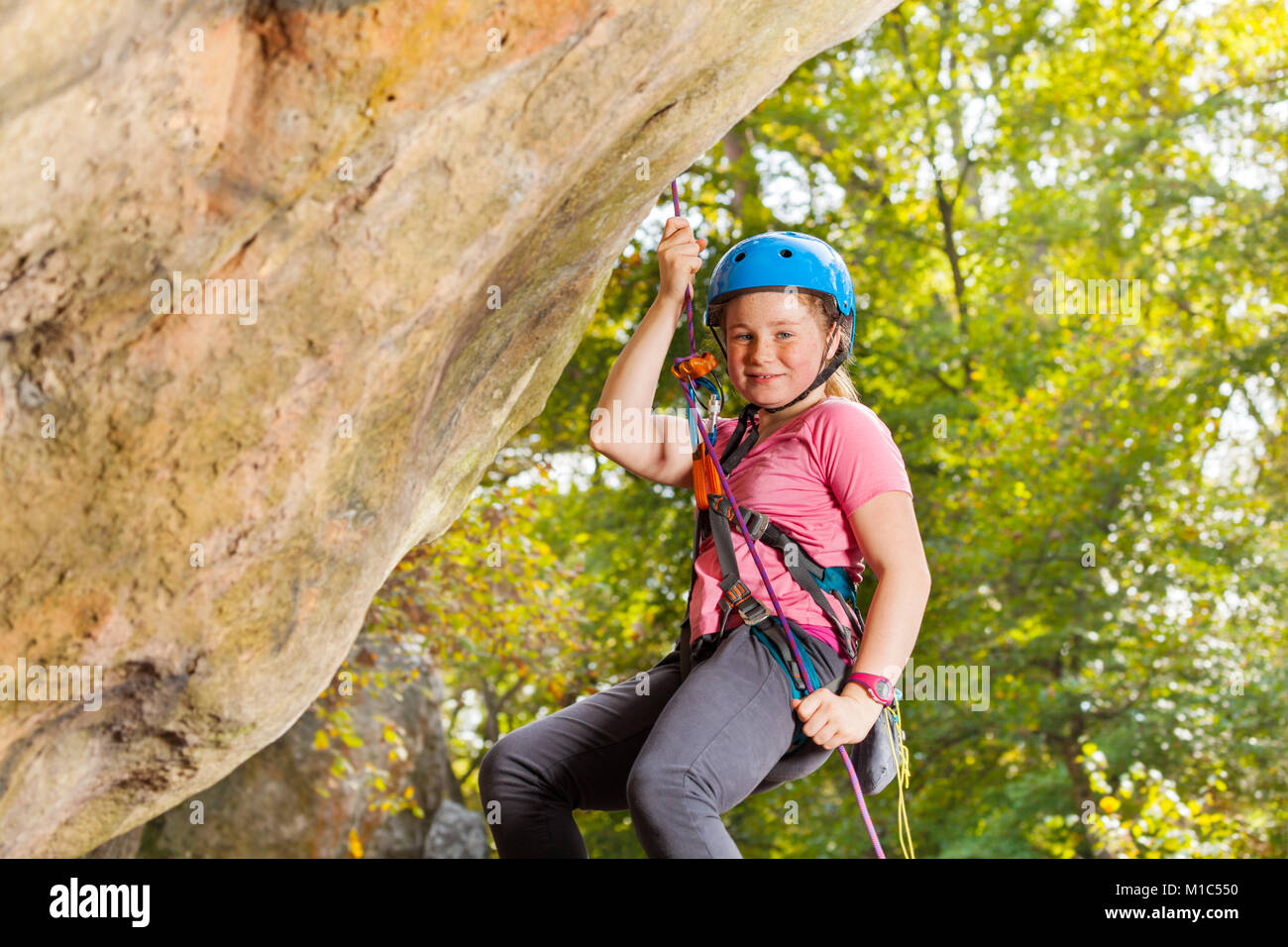 Portrait of teenage girl, rock climber in helmet, abseiling in forest ...