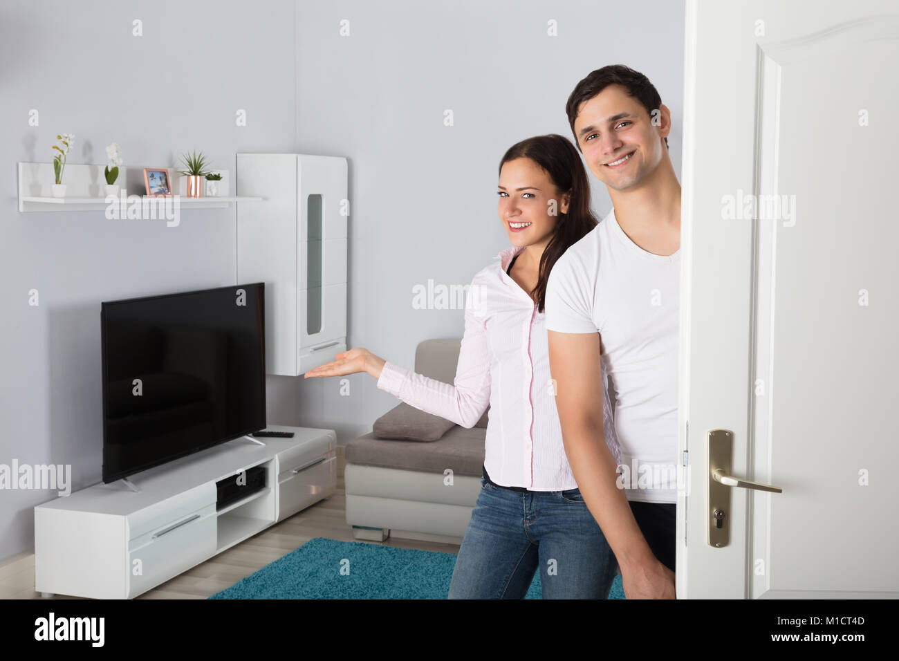 Portrait Of A Happy Young Couple Inviting People To Enter In Home Stock ...
