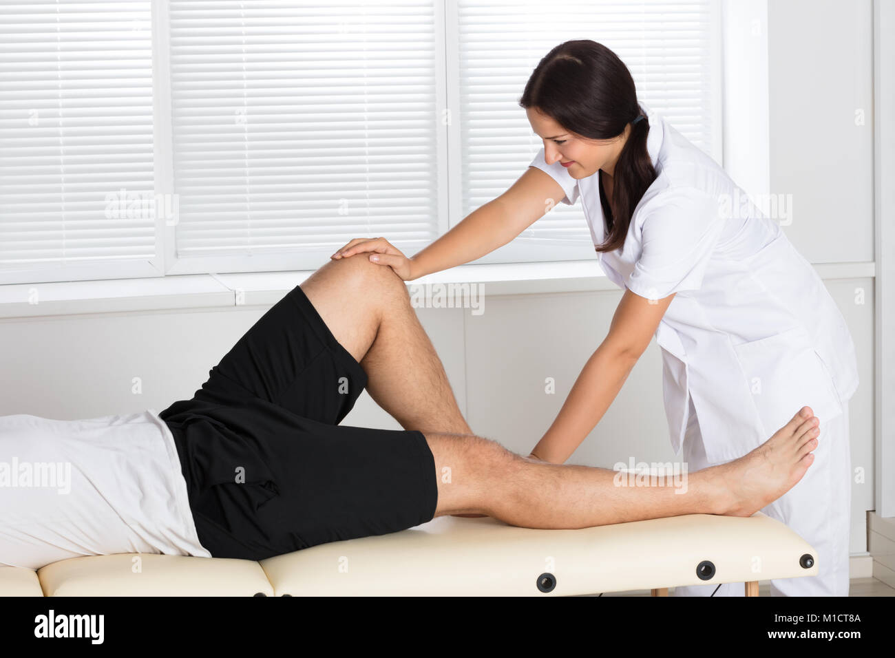 Young Female Physiotherapist Giving Leg Exercise To Patient In Clinic ...