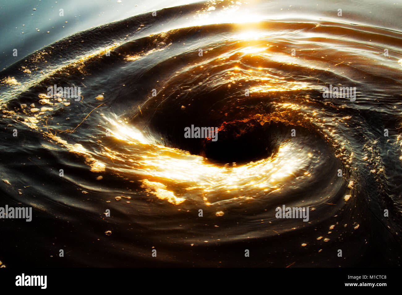 A small swirling circular motion of a water whirlpool with sunlight ...