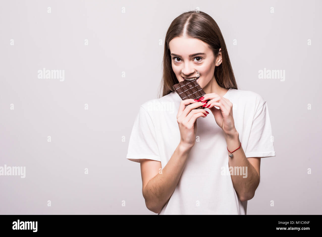 Young woman bites off slice from chocolate bar, on white background ...