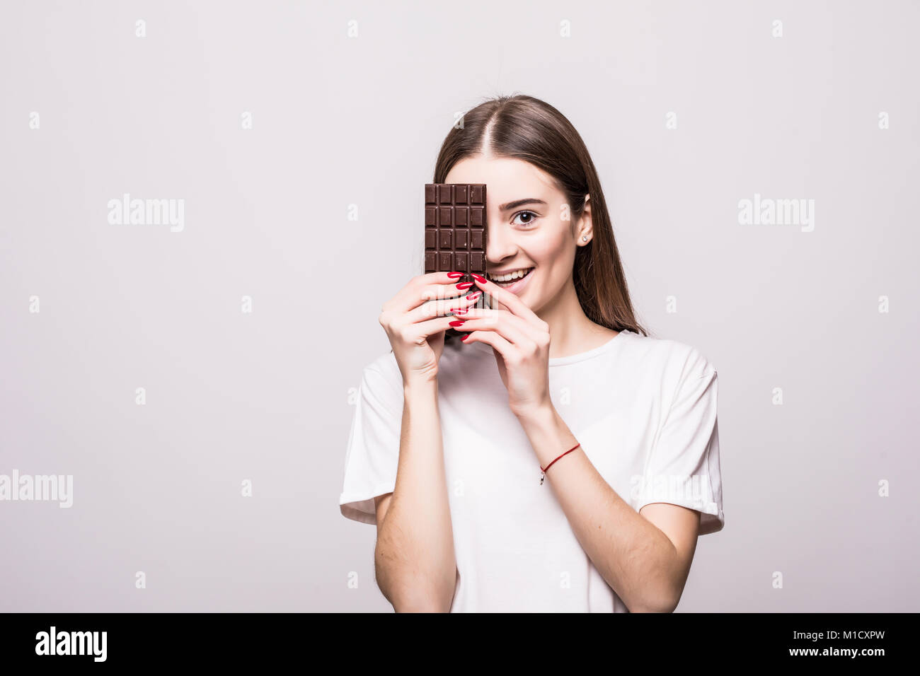 Young woman bites off slice from chocolate bar, on white background ...