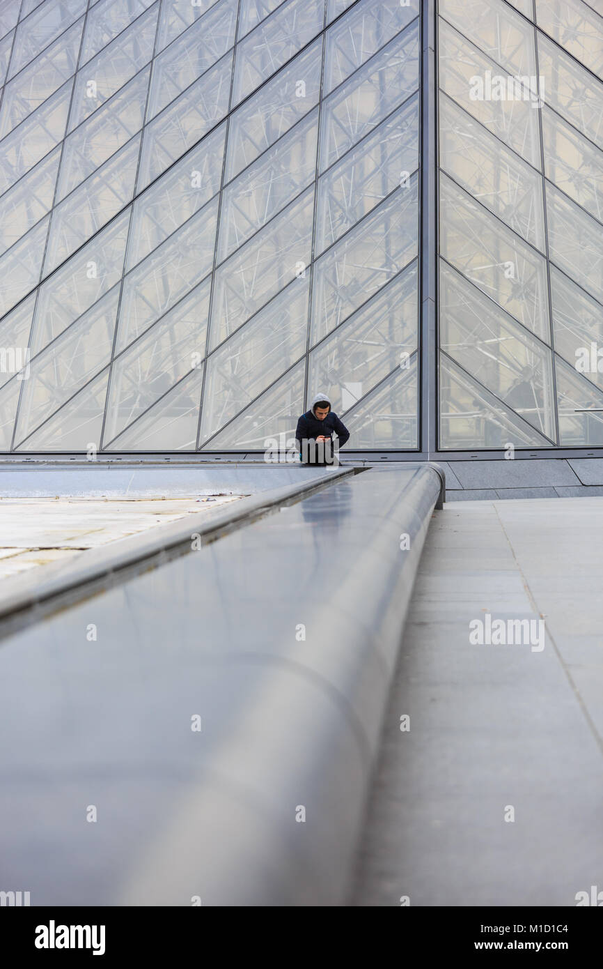 A man sits at the bottom of the famous glass pyramid entrance, looking ...