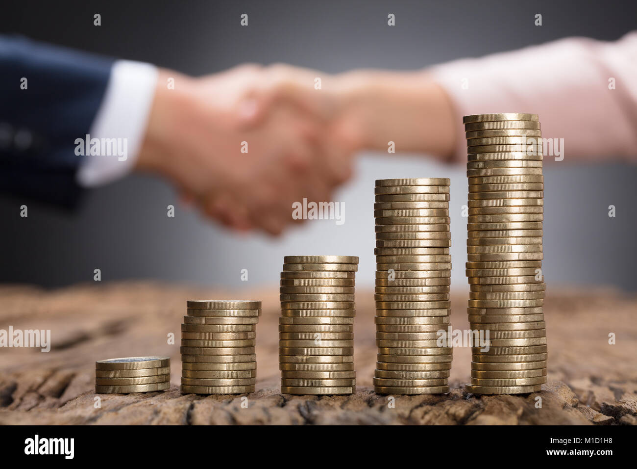 Close-up Of Stacked Coins In Front Of Businesspeople Shaking Hands ...