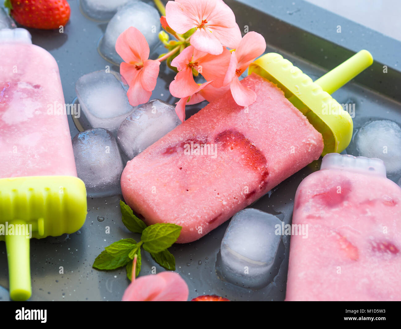 Home made strawberry ice cream popsicles on metall tray with ice cubes ...