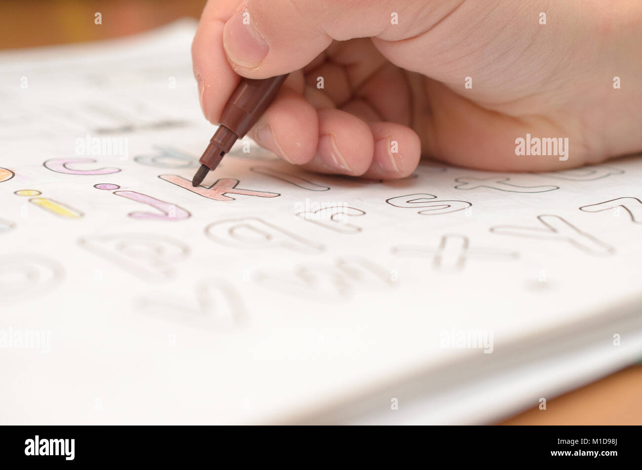A child's hand writes and displays English letters in a notebook and ...
