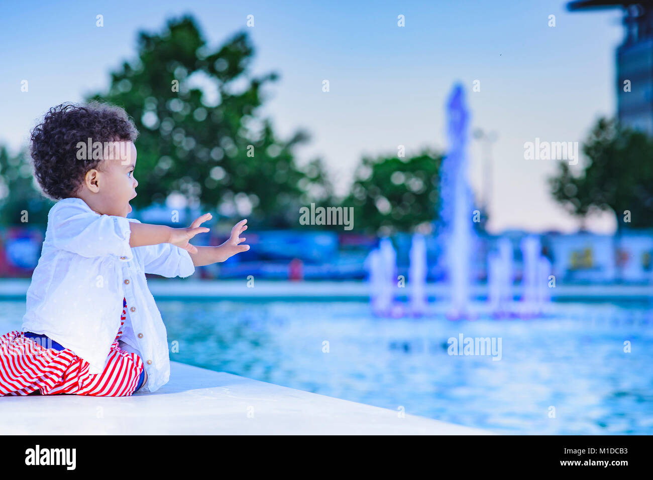 Cute baby girl playing next to fountain sprinklers Stock Photo - Alamy