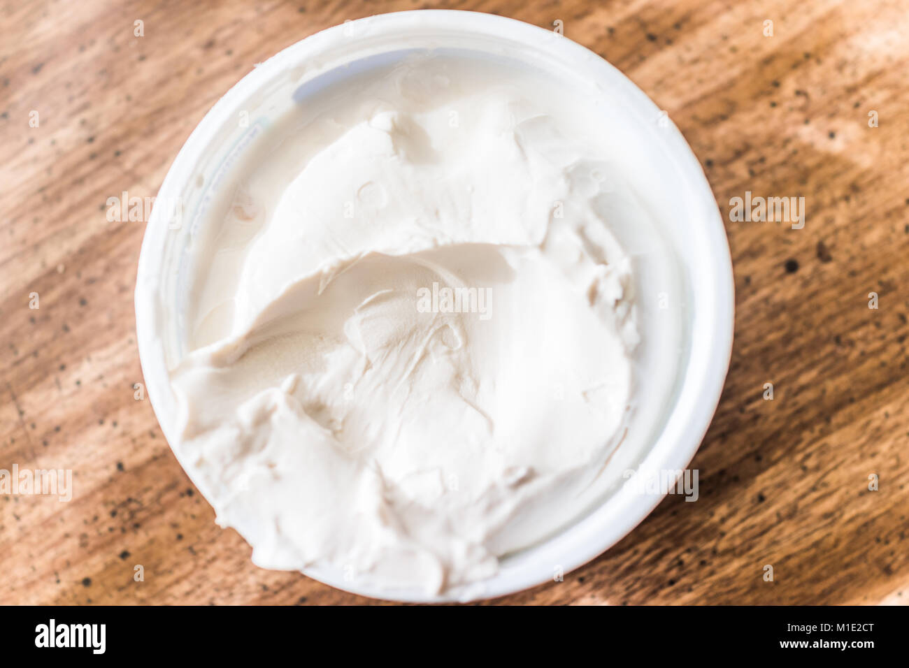 Closeup of small tub plastic container of white cream cheese on table ...