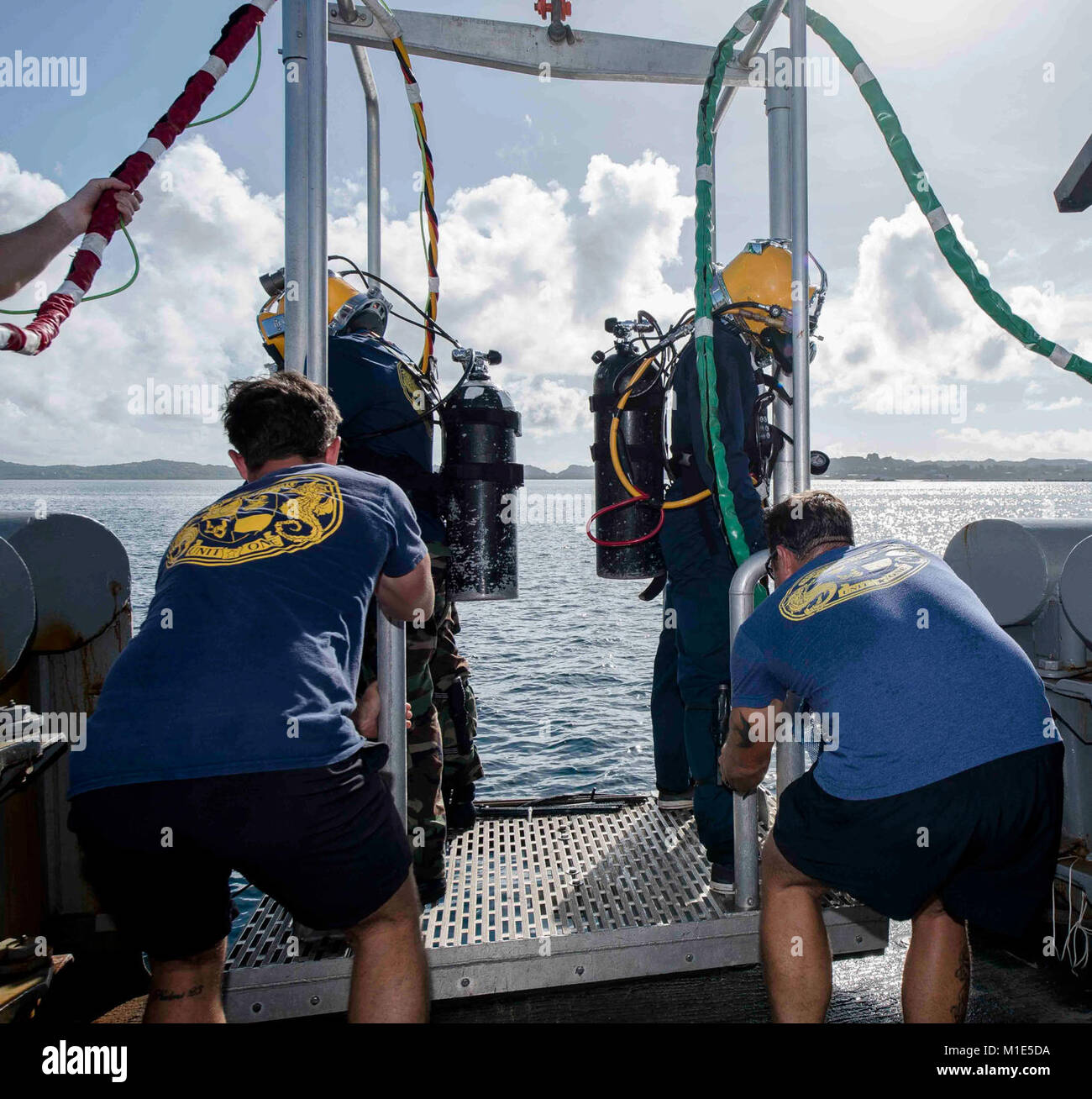 U.S. Navy Divers assigned to Mobile Diving and Salvage Unit One lower a ...