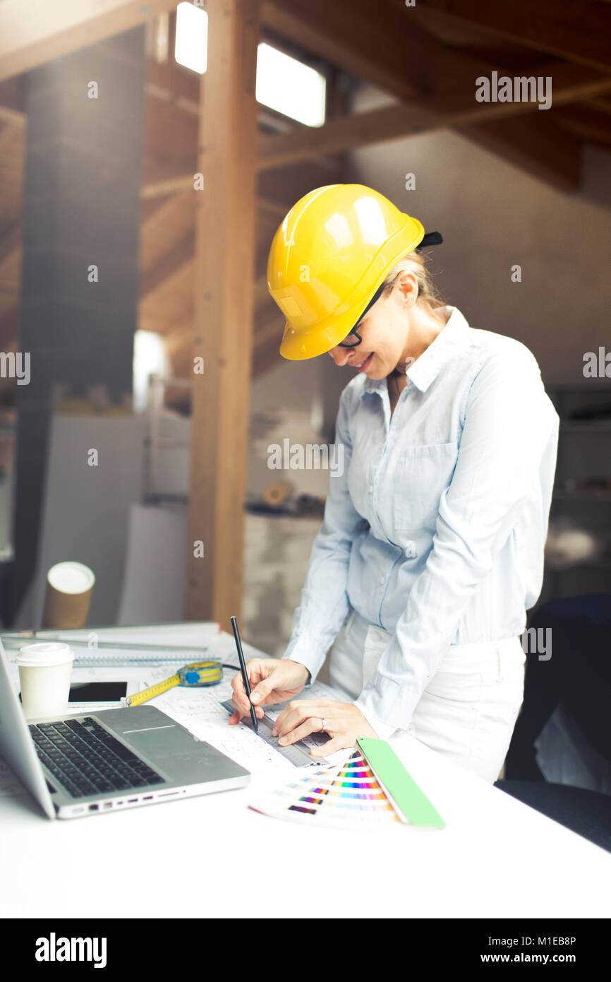 very pretty young female architect wearing yellow helmet is planning a loft in a house Stock ...