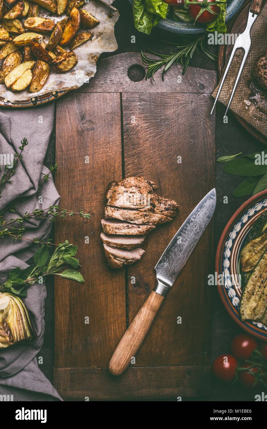Sliced fried pork meat and kitchen knife on cutting board with baked ...