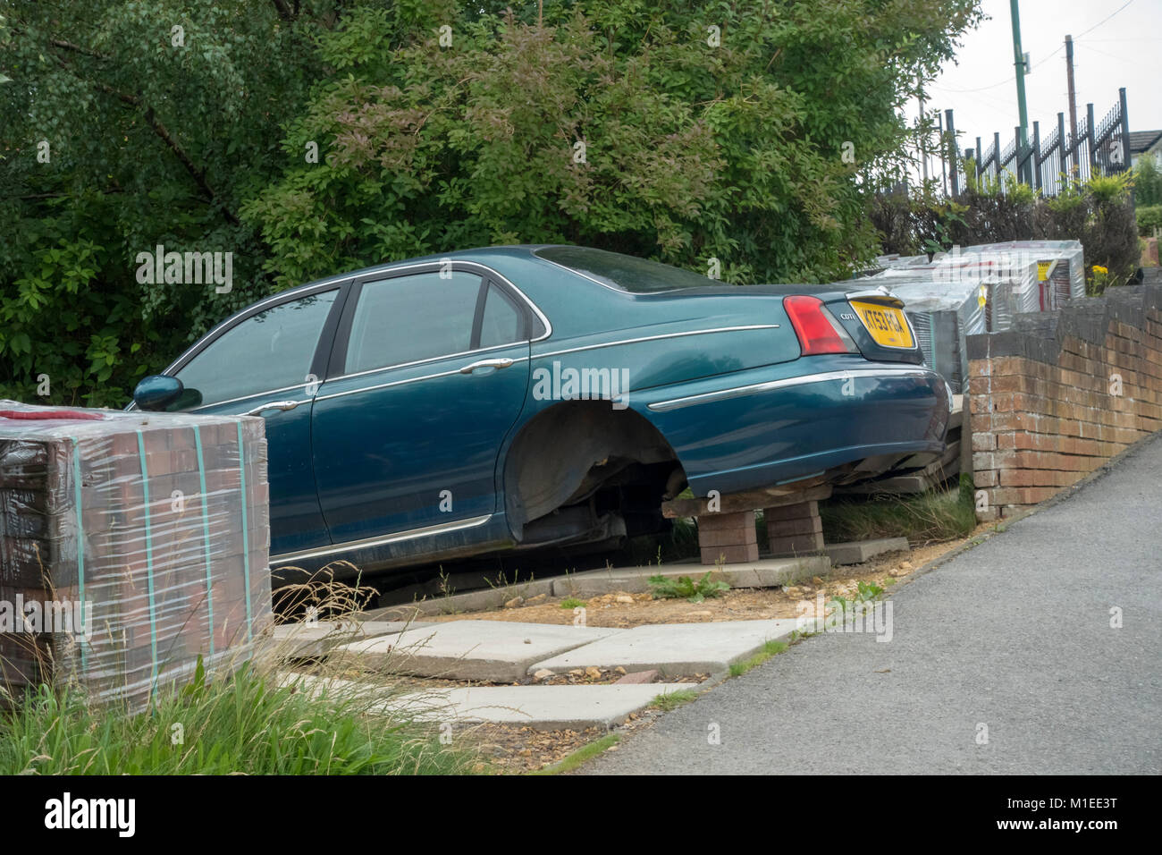 A green Rover 75 car in a driveway, up on bricks with it's rear axle ...