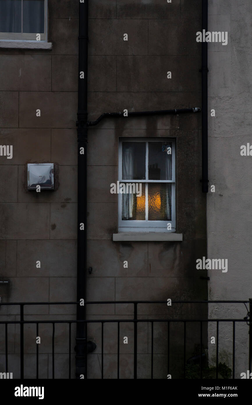A small window at the back of a run down house glows from the inside ...