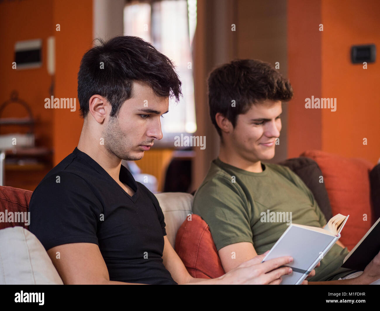 Two casual young men posing on couch concentrated on reading books at ...