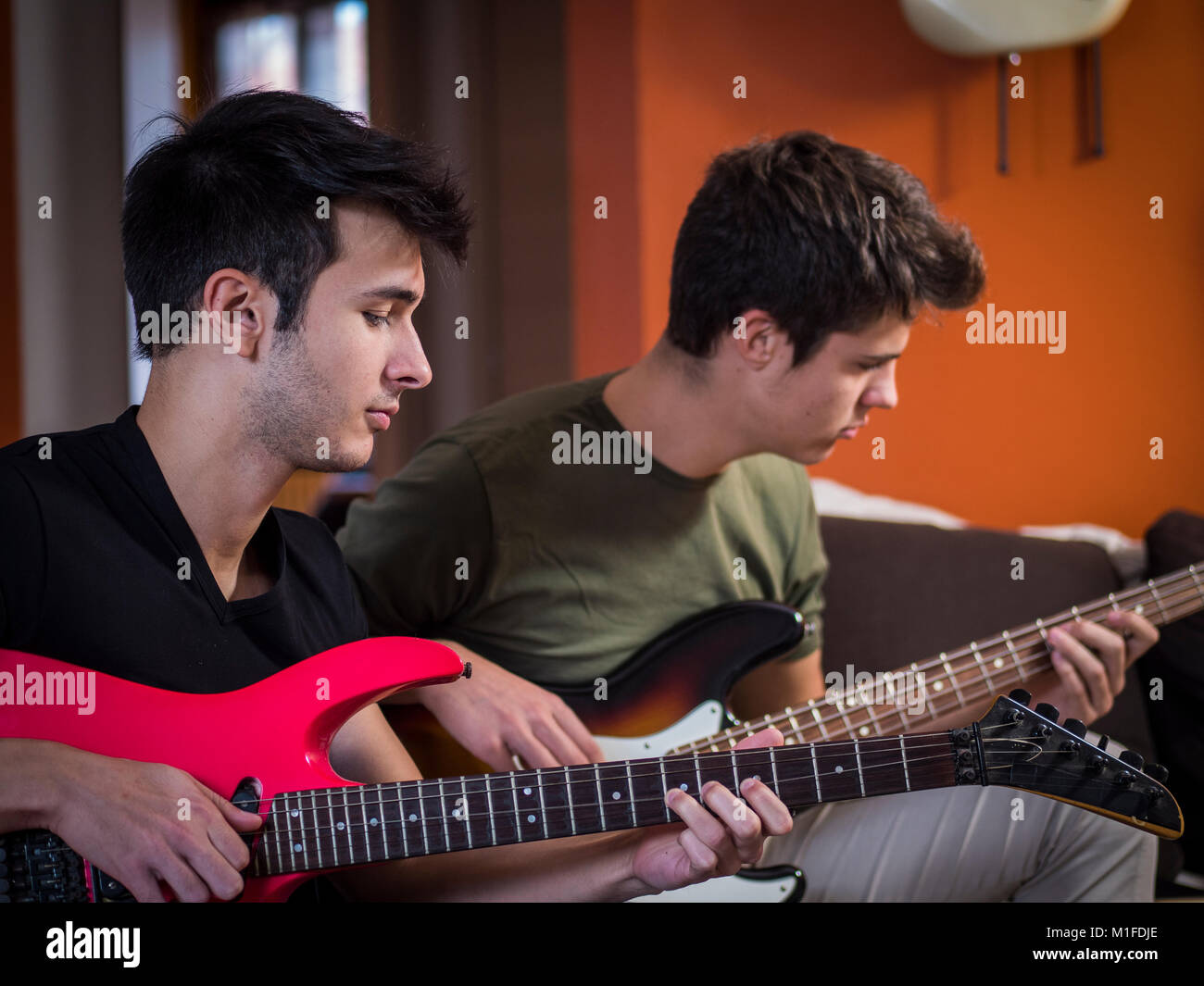 Two casual guys posing on sofa and playing electric guitar and bass in ...