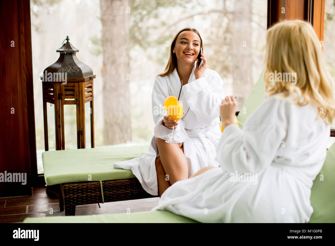 Two cheerful women in bathrobes drinking juice in spa center Stock ...