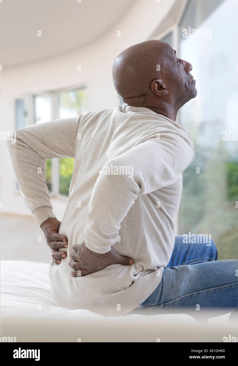 African American man with severe backache sitting on bed in his luxery ...