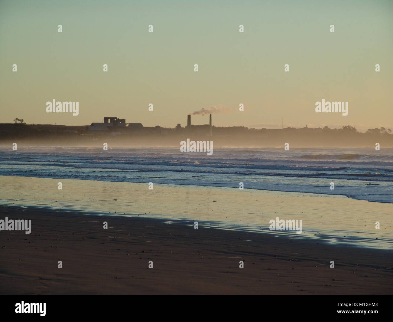 Distant factory, far behind the beach. Sunset Stock Photo - Alamy