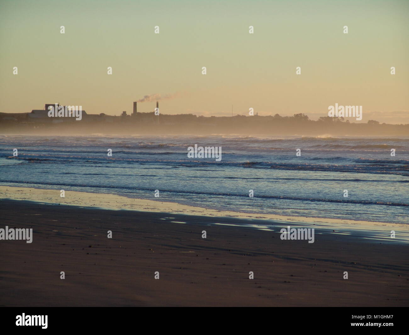 Distant factory, far behind the beach. Sunset Stock Photo - Alamy