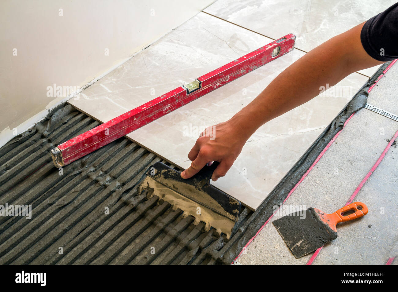Ceramic tiles and tools for tiler. Worker hand installing floor tiles ...