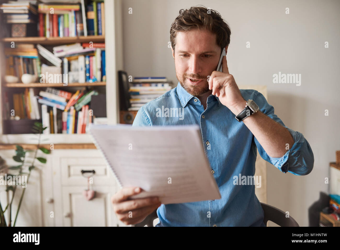 Man reading paperwork and talking on a cellphone at home Stock Photo ...