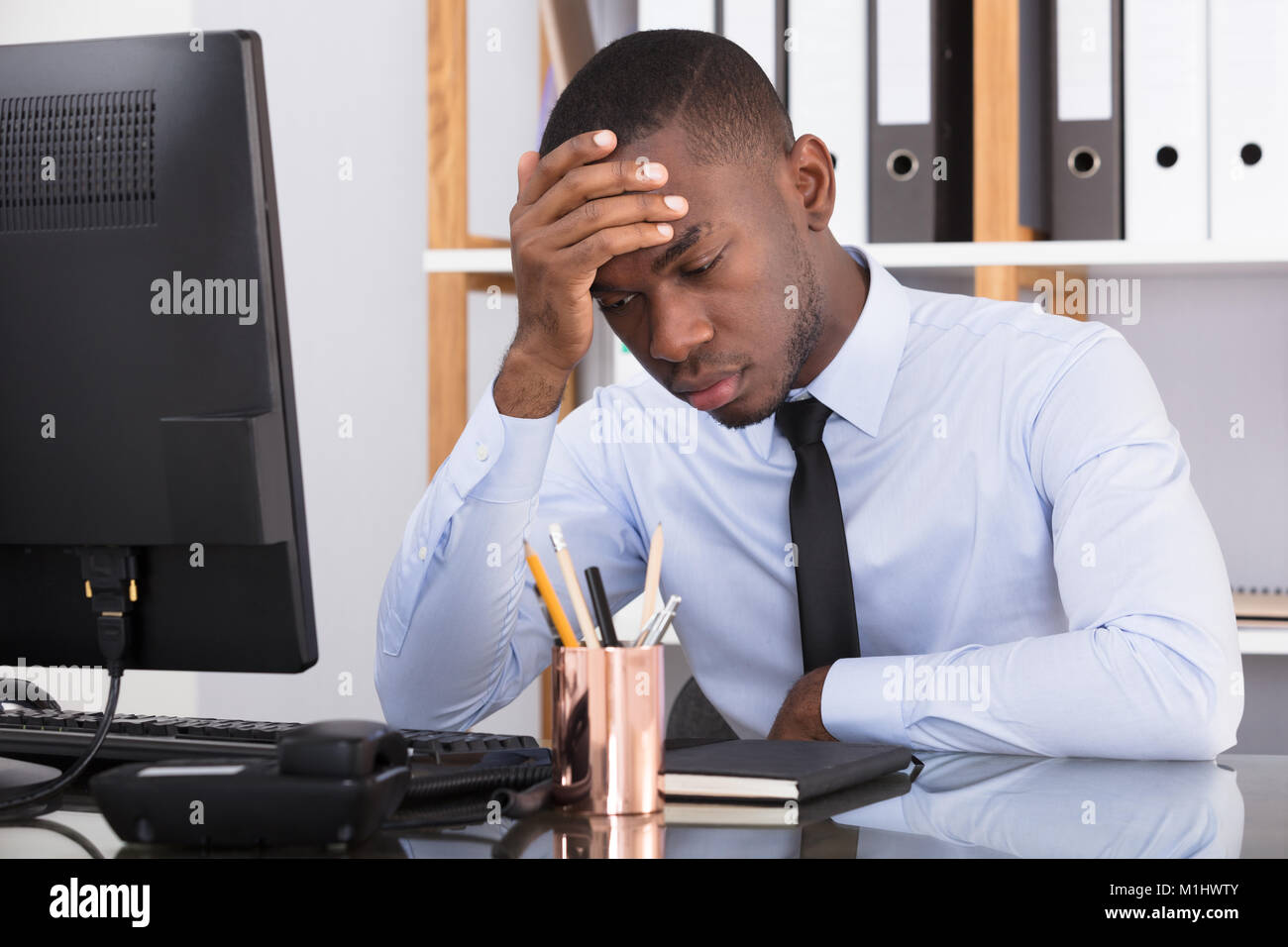 Stressed Male Businessman Sitting With Head In Hand At Desk In Office ...