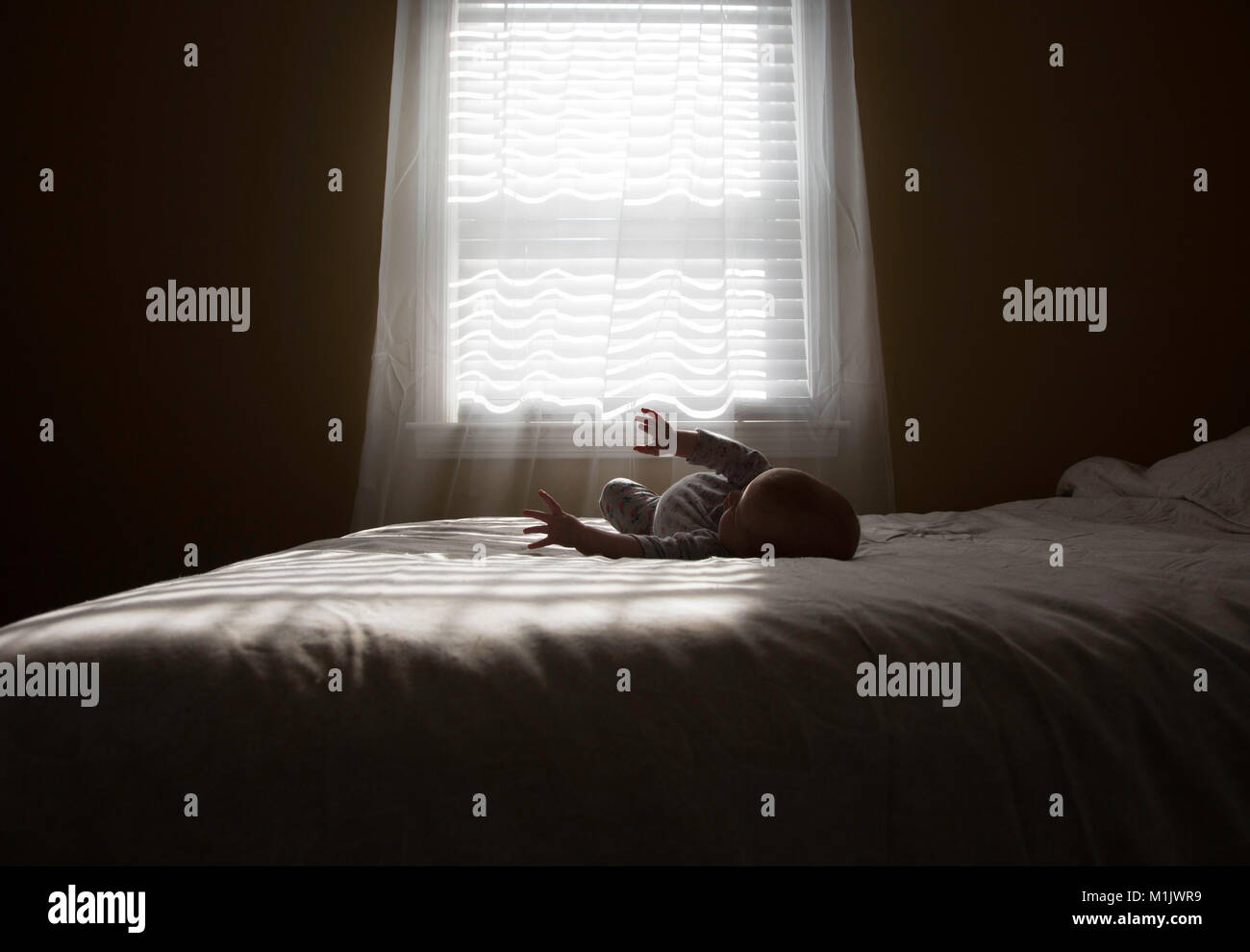 Baby Laying on Bed in front of Window Stock Photo - Alamy