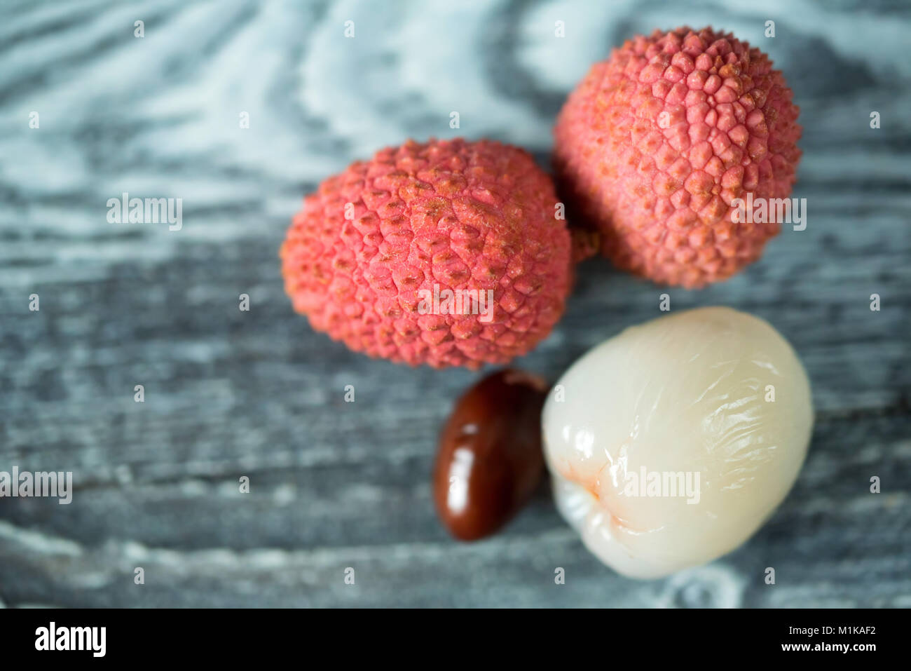 Three lychee fruits and seed on wooden background Stock Photo - Alamy