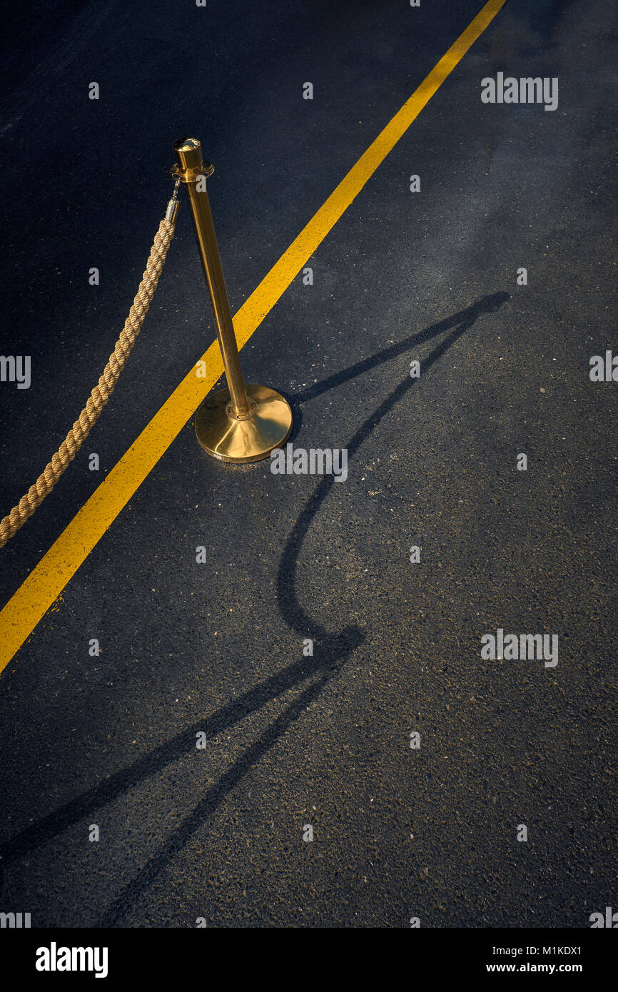 A gold rope barrier and stand on a road with a single yellow line and ...