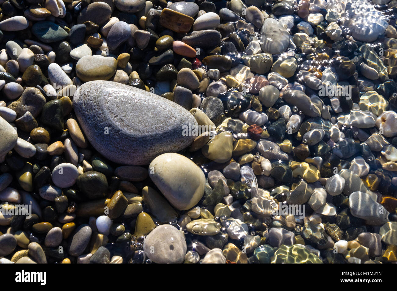 sea pebble beach with multicoloured stones, transparent waves with foam ...