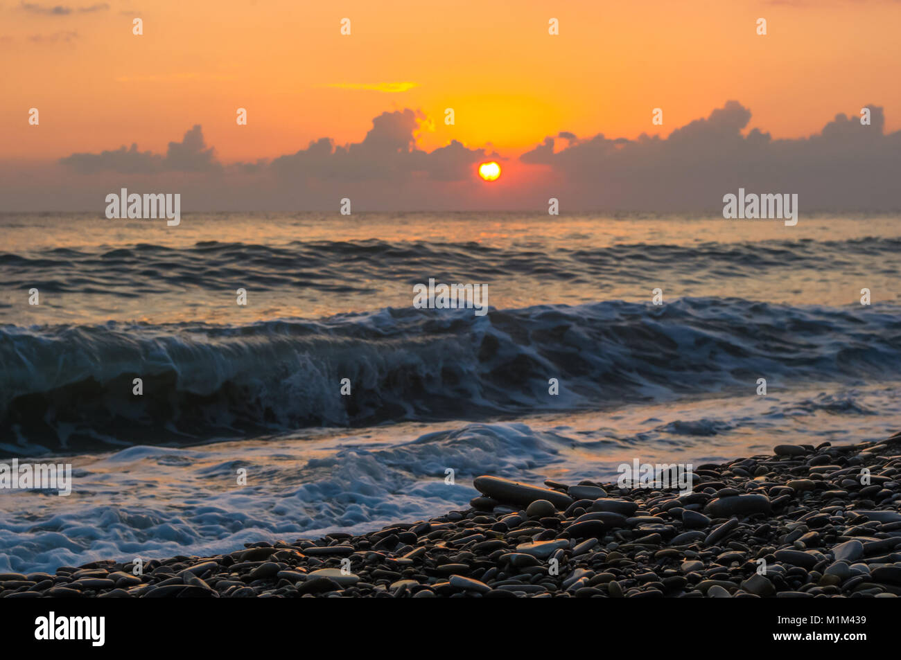 Summer sea sunset on the pebble beach, the sun, waves and clouds ...