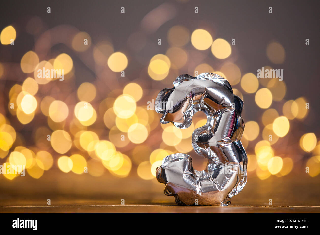 Silver number 3 celebration foil balloon against blurred light ...