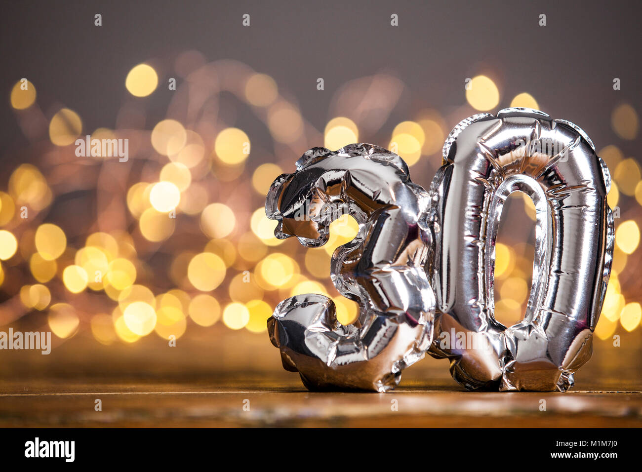 Silver number 30 celebration foil balloon against blurred light ...