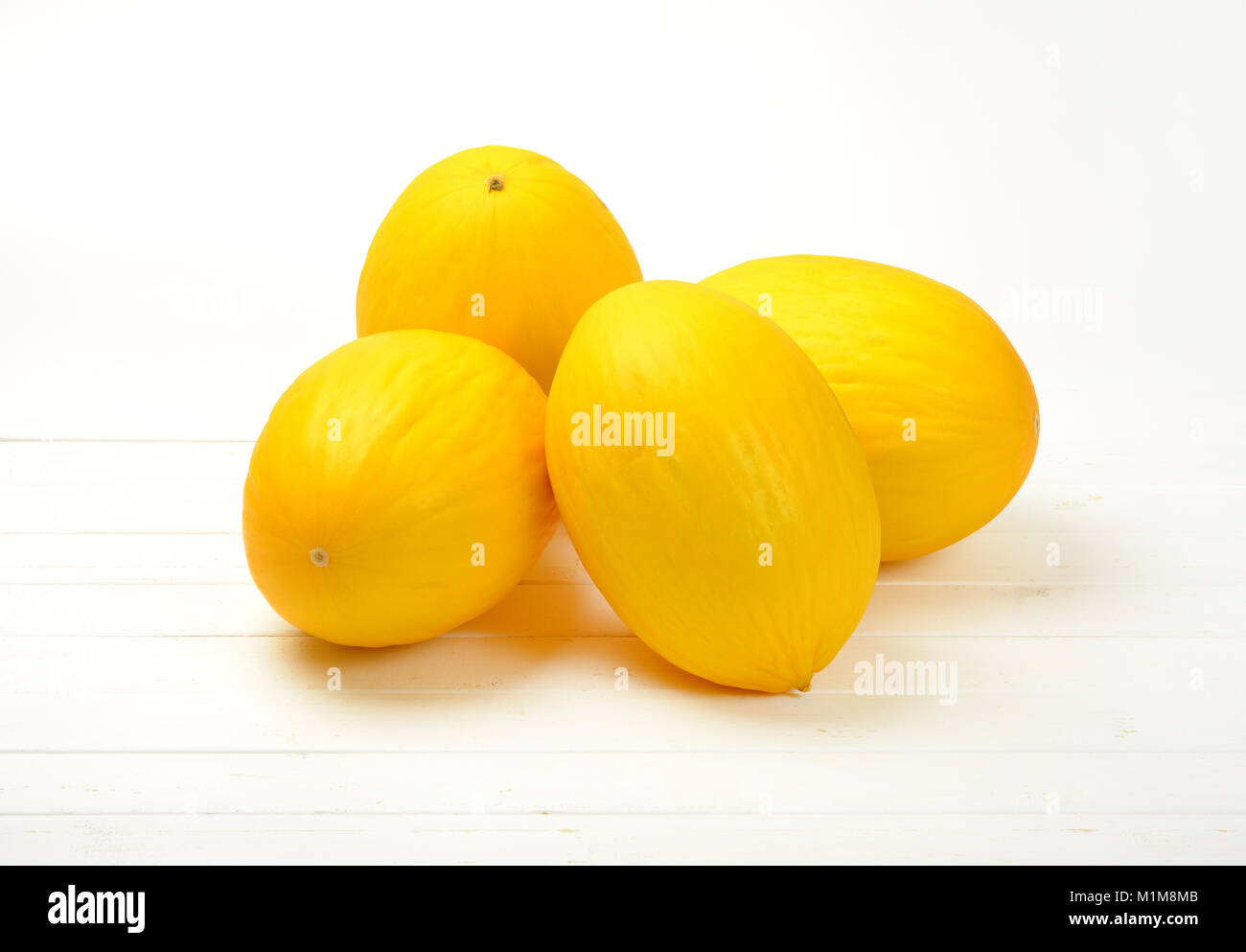 four whole yellow melons on white wooden background Stock Photo - Alamy