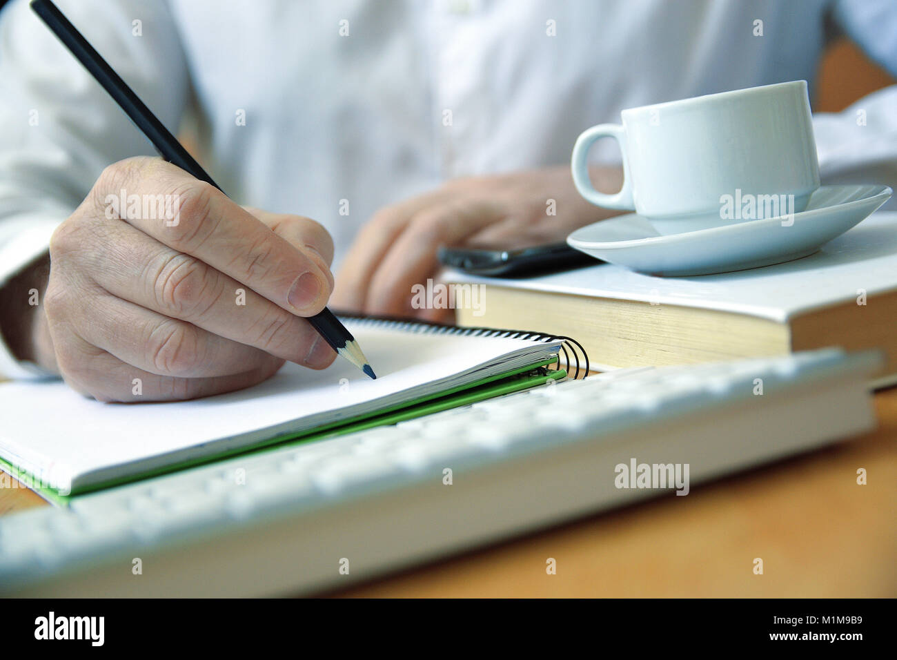 Young business man writing notes at the office taking a cup of coffee ...