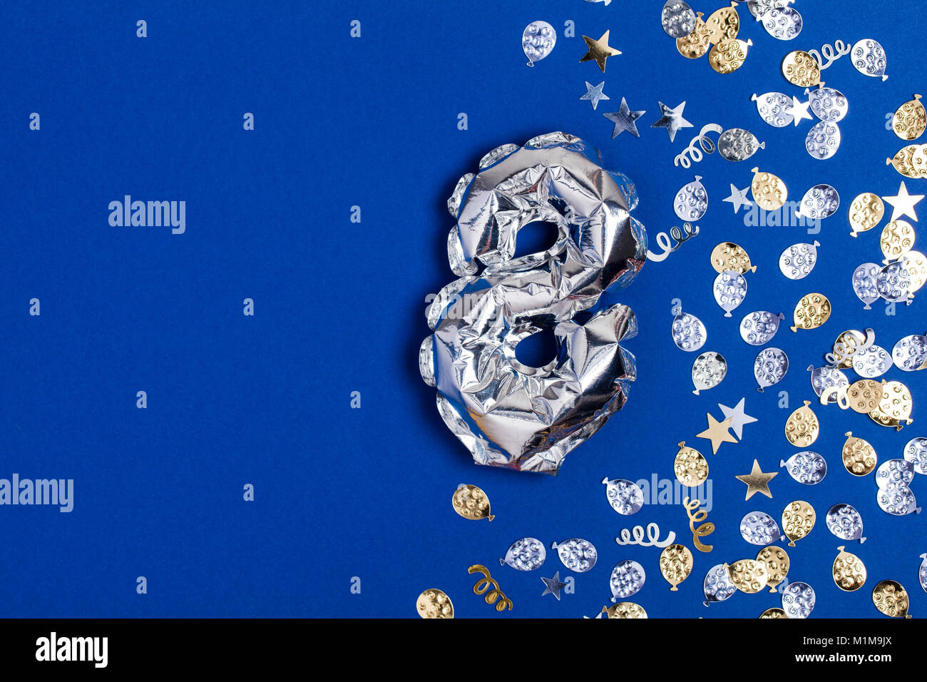 Silver foil number 8 balloon on a blue background with glitter gonfetti ...