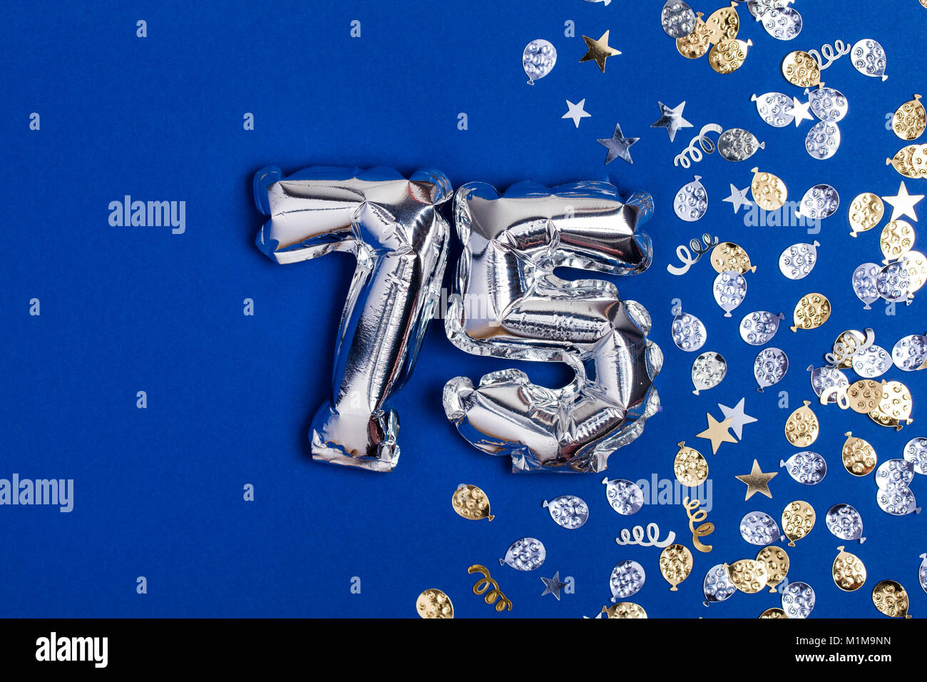 Silver foil number 75 balloon on a blue background with glitter ...