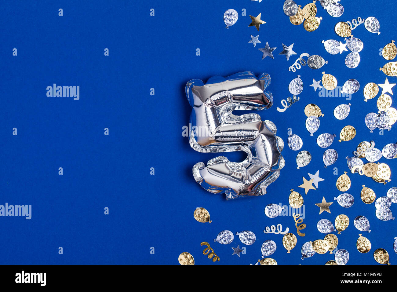 Silver foil number 5 balloon on a blue background with glitter gonfetti ...